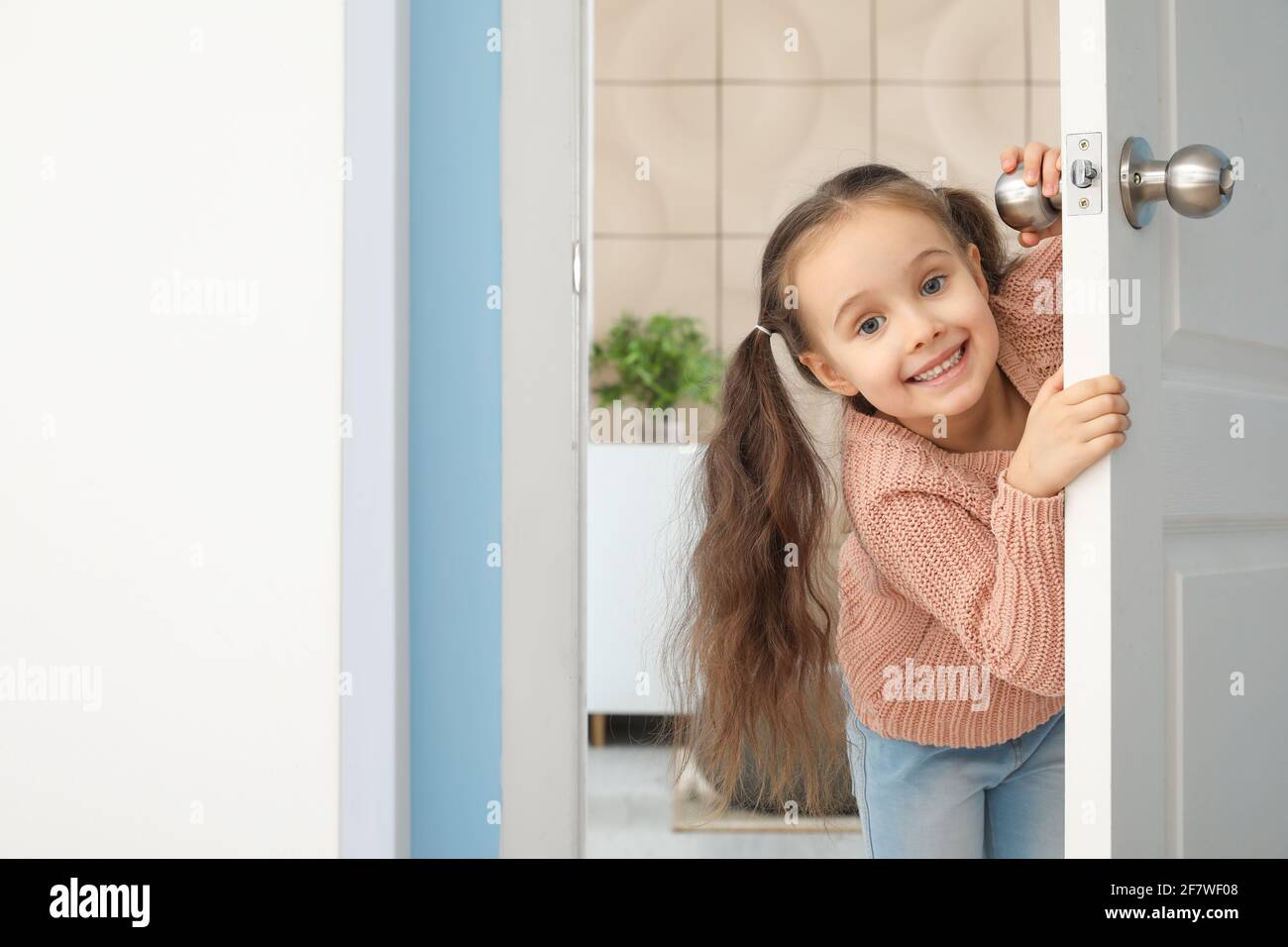 Cute little girl looking out the door Stock Photo - Alamy