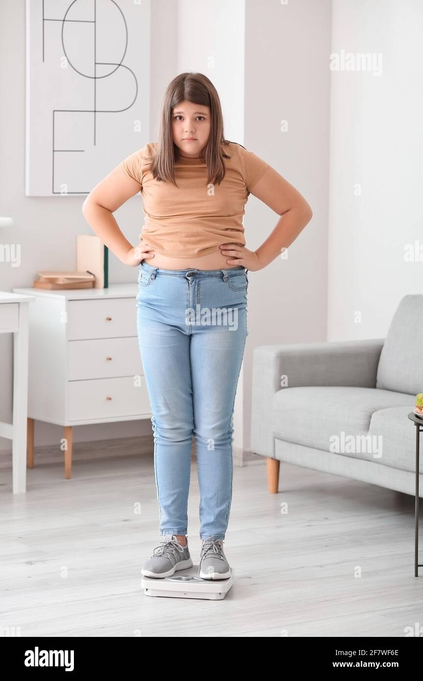 Sad overweight girl standing on measuring scales at home Stock Photo ...