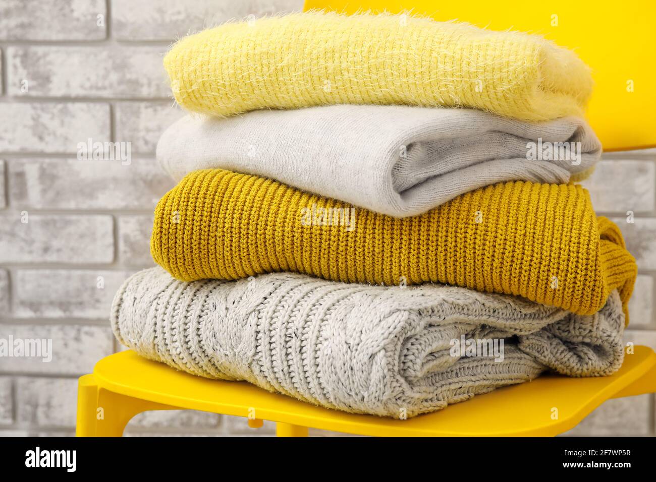 Chair with stack of stylish clothes on brick background Stock Photo - Alamy