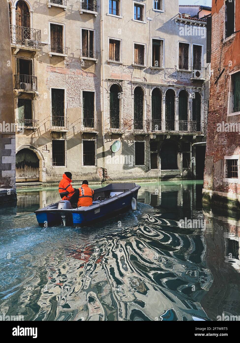 Two orange workers wearing a uniform going to work on boat in Venice ...