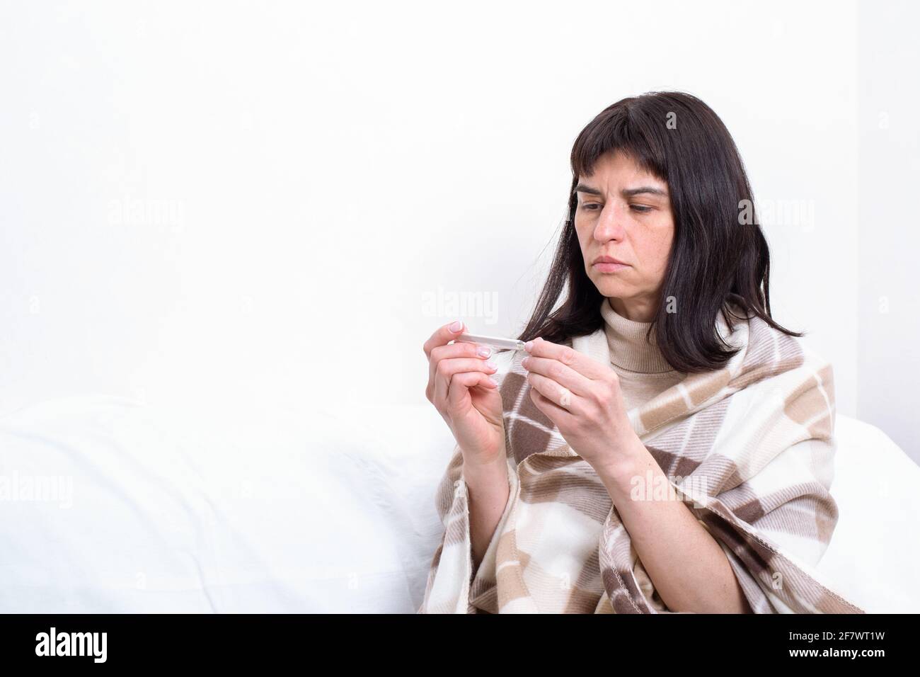 Sick day at home. Sick woman covered with a blanket holds a thermometer ...