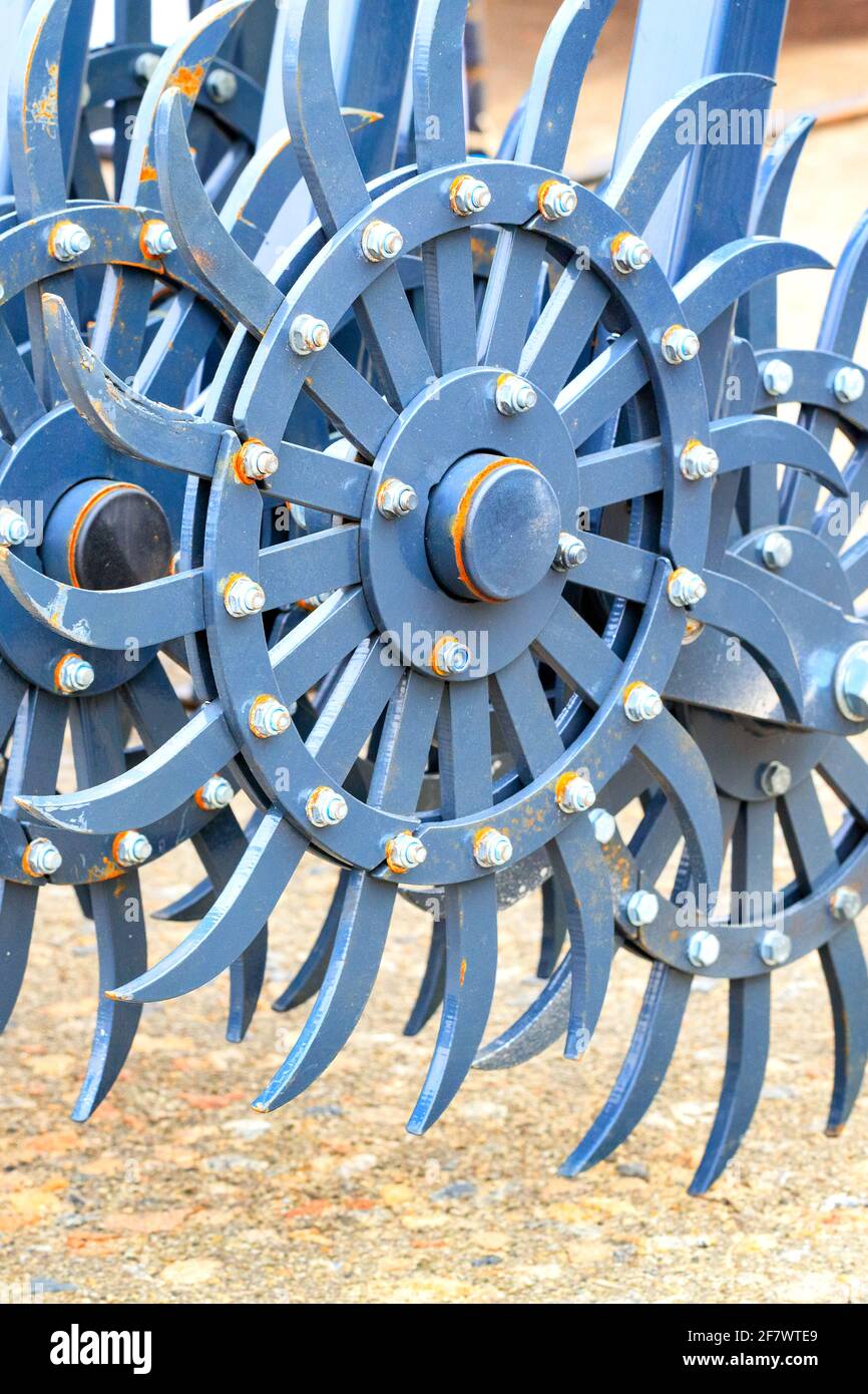 A toothed metal harrow of blue color on the hitch of a tractor for ...