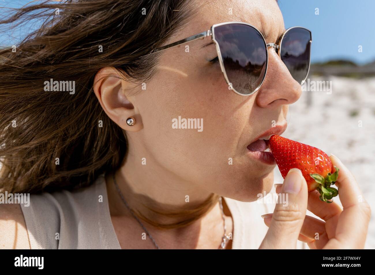 Close-up caucasian woman biting a strawberry. Girl in nature wearing ...
