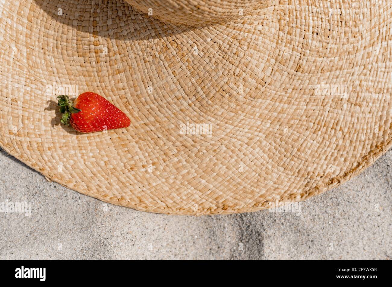 A ripe strawberry on a cropped straw hat on the sand. Shot from above ...