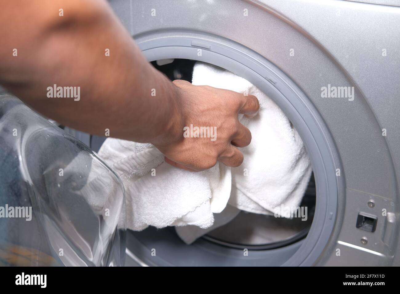 young man putting towel into washing machine Stock Photo - Alamy