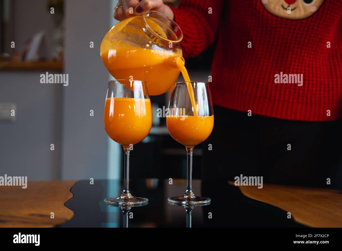 Female in a red jumper pours fresh carrot juice into wine glasses Stock ...