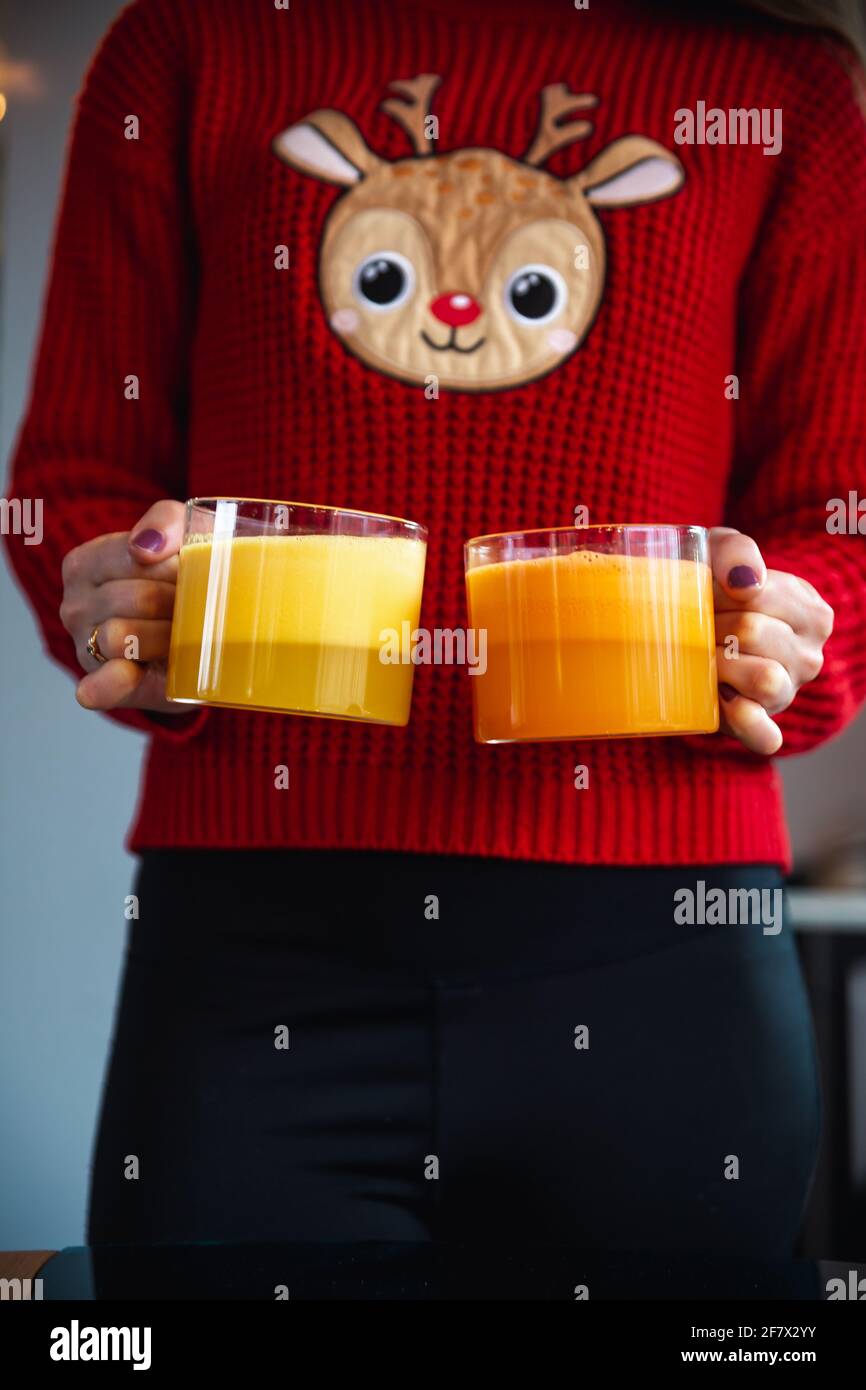 Female in red jumper holding glass cups with fresh carrot and orange ...