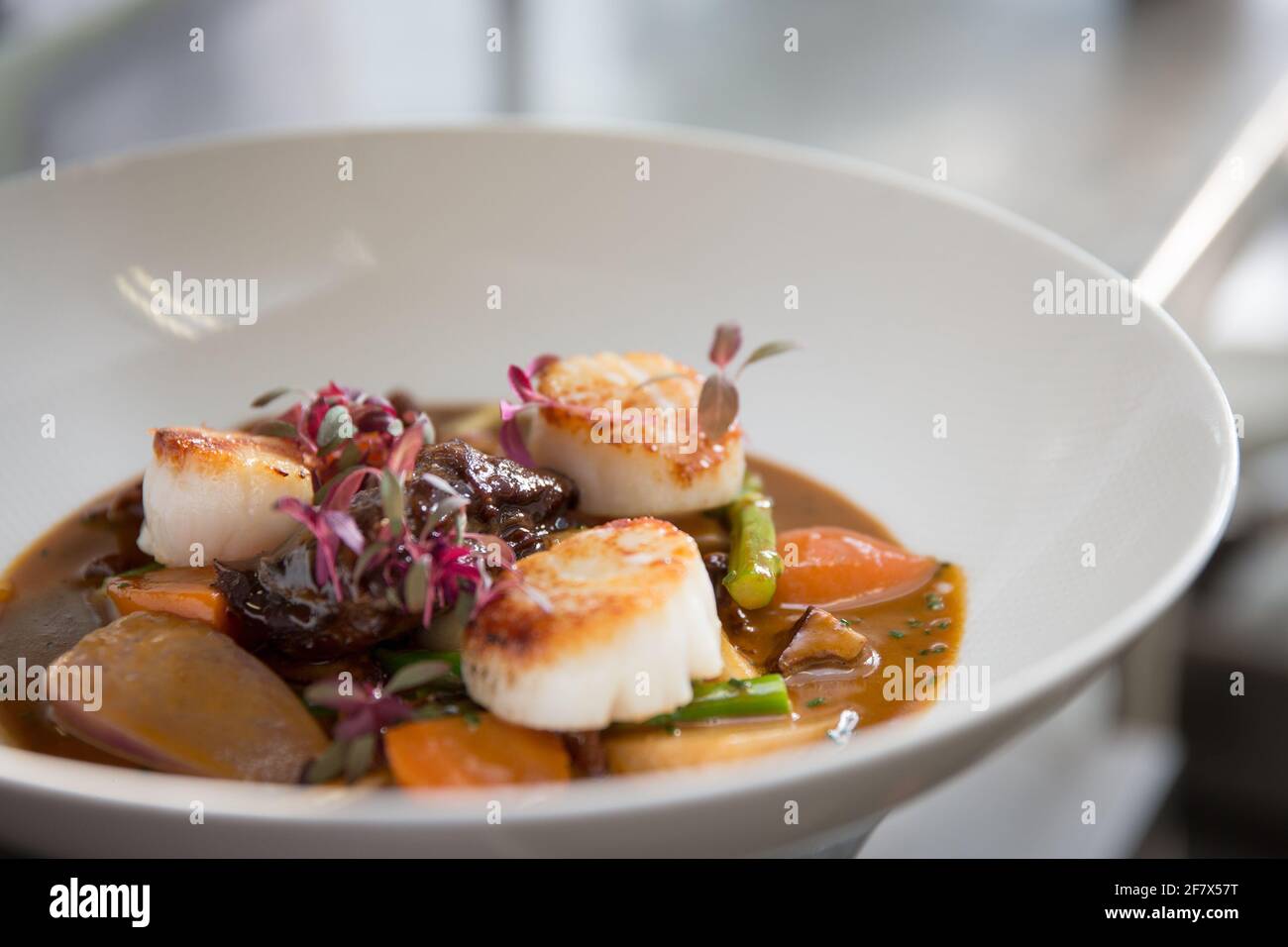 A fancy fine dining dish bowl sitting on edge of stainless steel ...