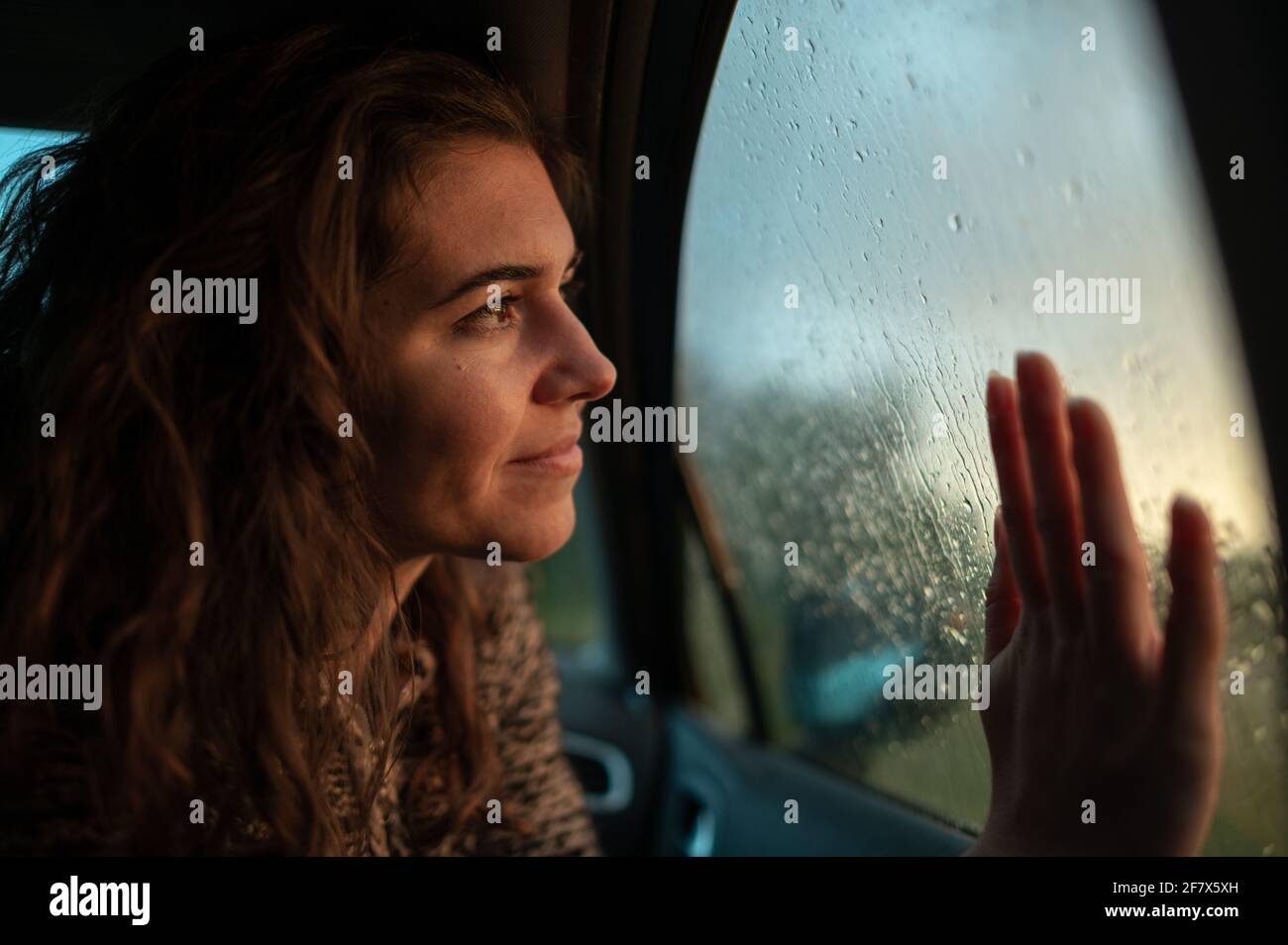 Portrait of young woman inside car while raining. Smiley face looking ...