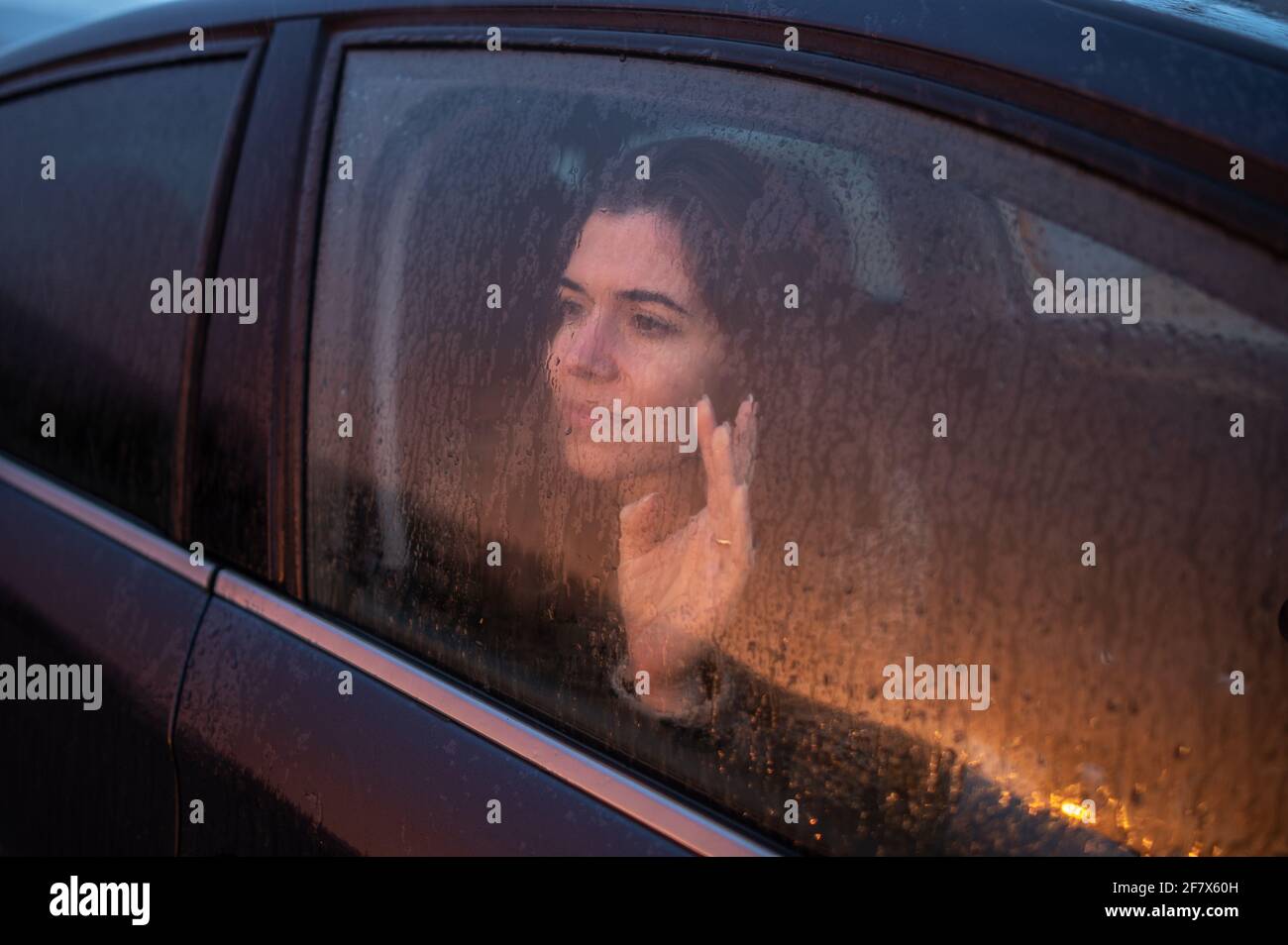 Close-up young woman inside car looking through window place hand on ...