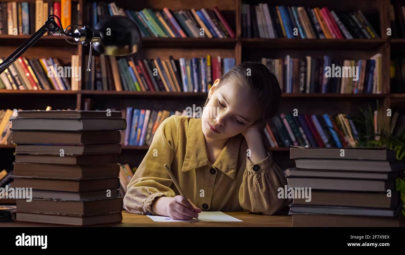 Tired girl writes home assignment on sheet of paper with pencil and ...