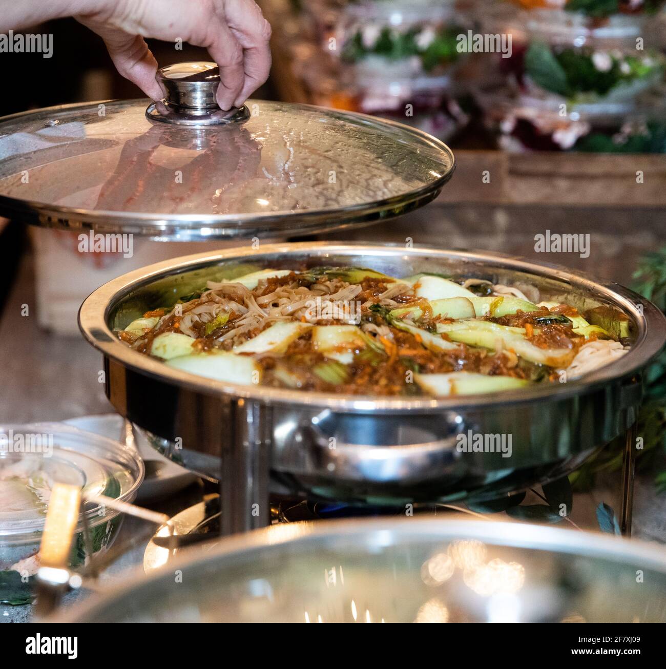 asian looking recipe in a metal plate on a buffet table with a hand ...