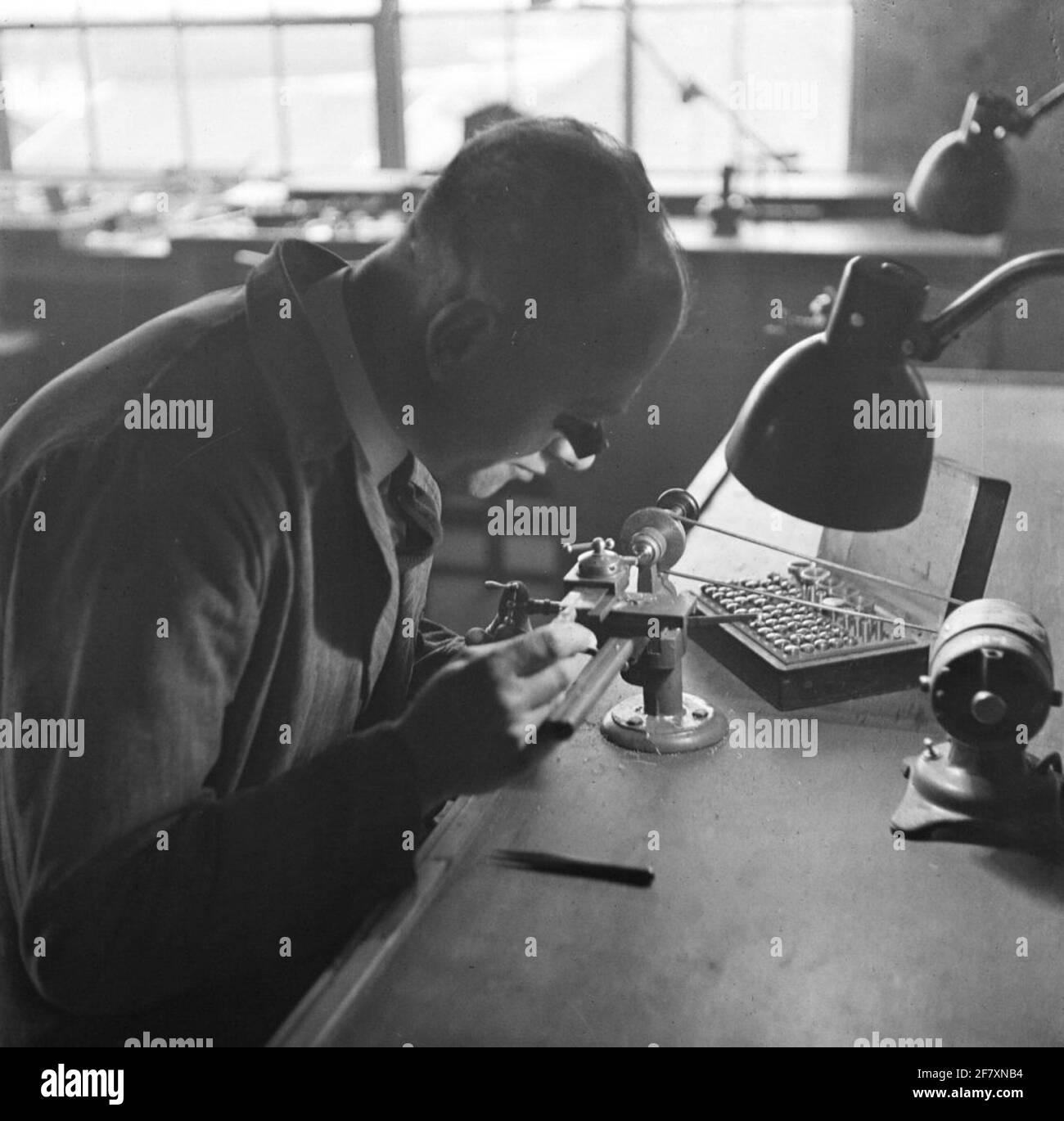 An instrument maker at work on a simple lathe with trays and loose ...