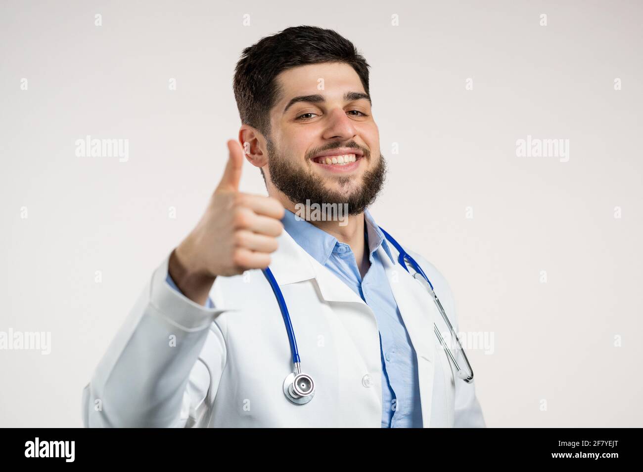 Doctor showing thumb up sign over white background. Positive young man ...