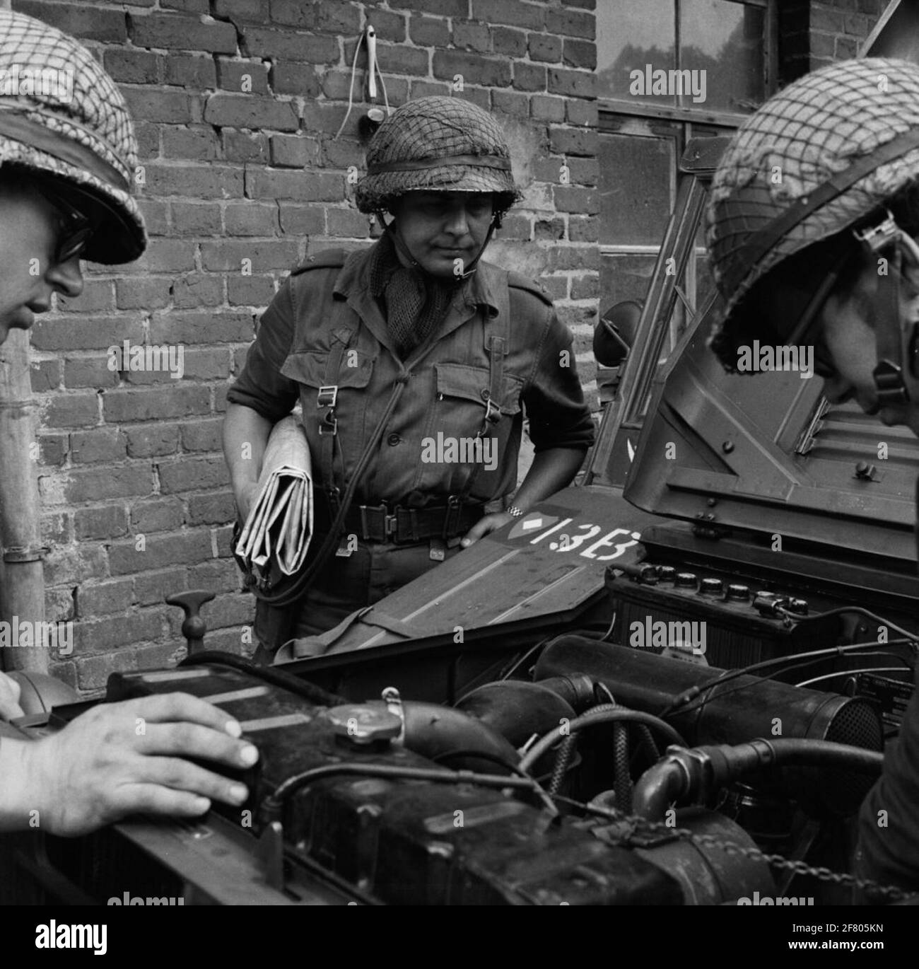Three soldiers of the royal army inspect the engine compartment of a ...