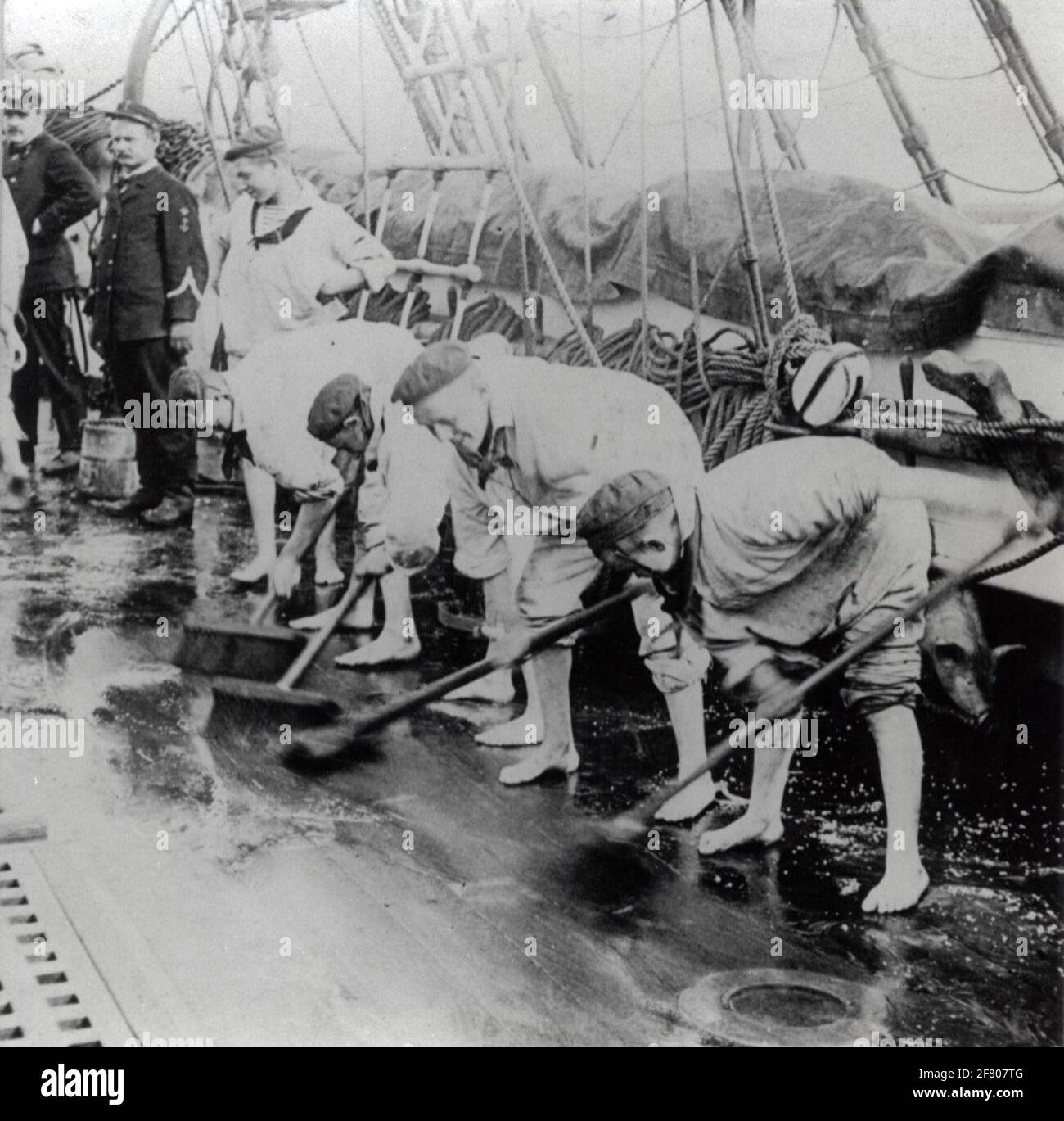 Crew members scrub the deck on board the instruction ship Zr./hr.ms ...