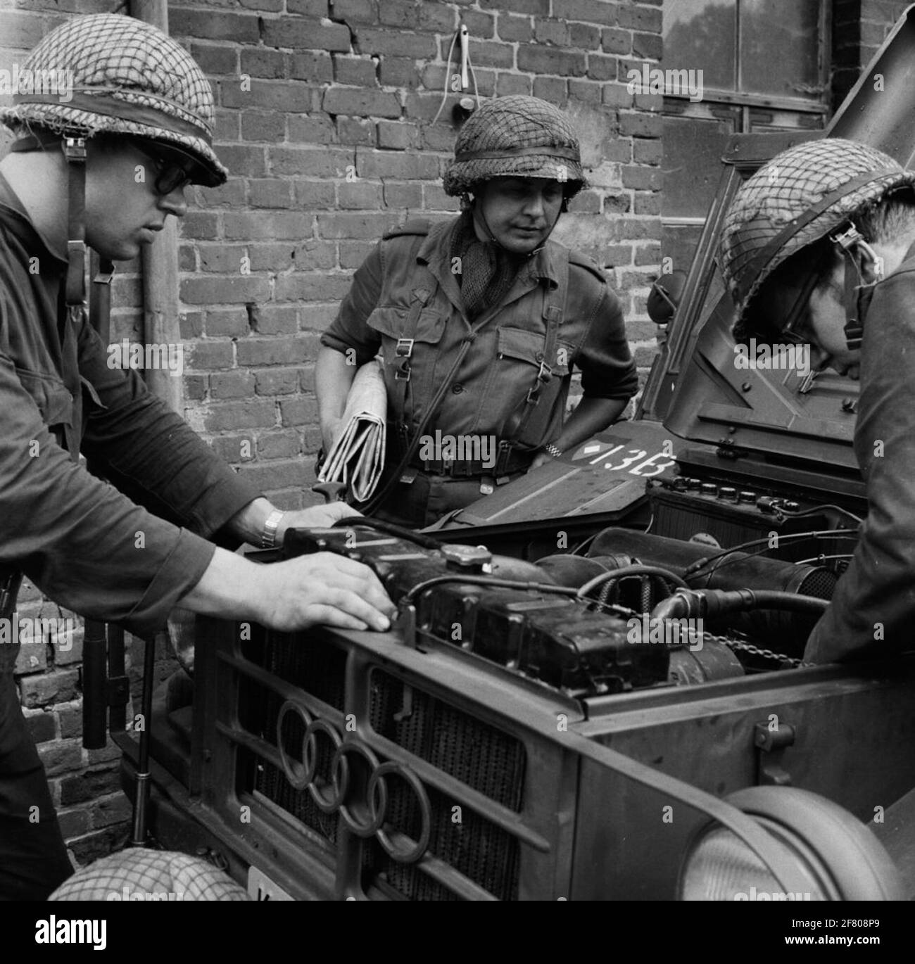 Three soldiers of the royal army inspect the engine compartment of a ...