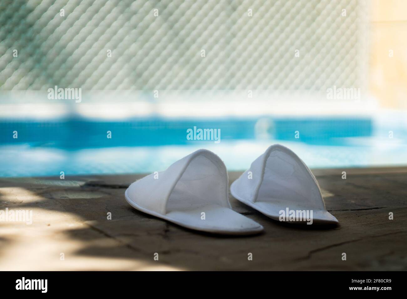 white cloth carpet sippers placed on the side of a out of focus pool ...