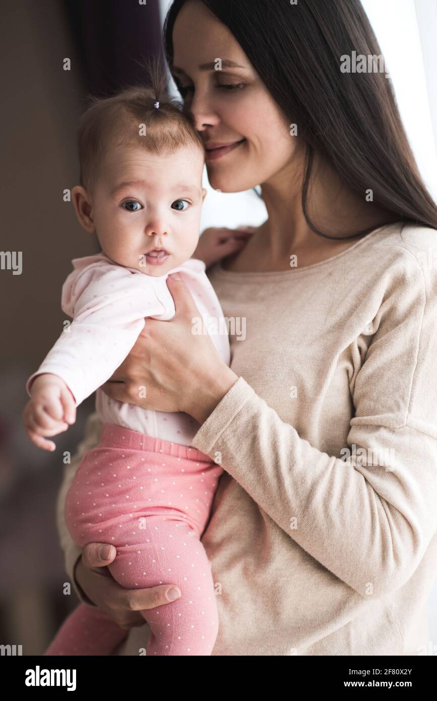 Mother holding baby girl at home. Newborn child on woman hands indoors. Motherhood. Maternity ...