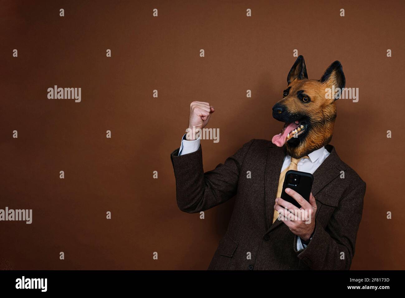 An elated man with smartphone and a latex dog head mask raising his ...