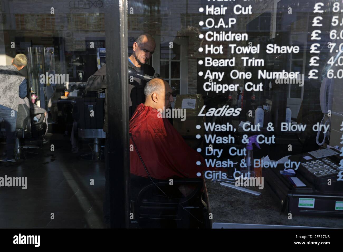 Board at barber shop with prices and barber in background drying the ...