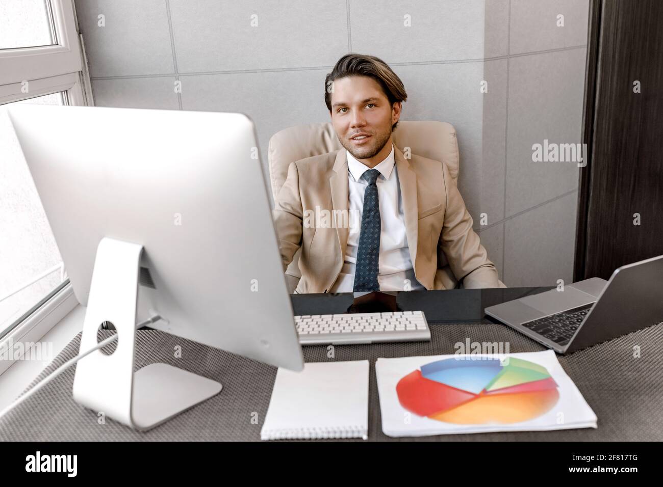 Handsome businessman in stylish suit is using computer, sitting at the ...