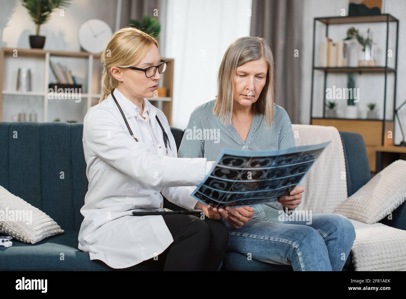 Doctor and senior woman looking at x-ray scan image during home visit ...