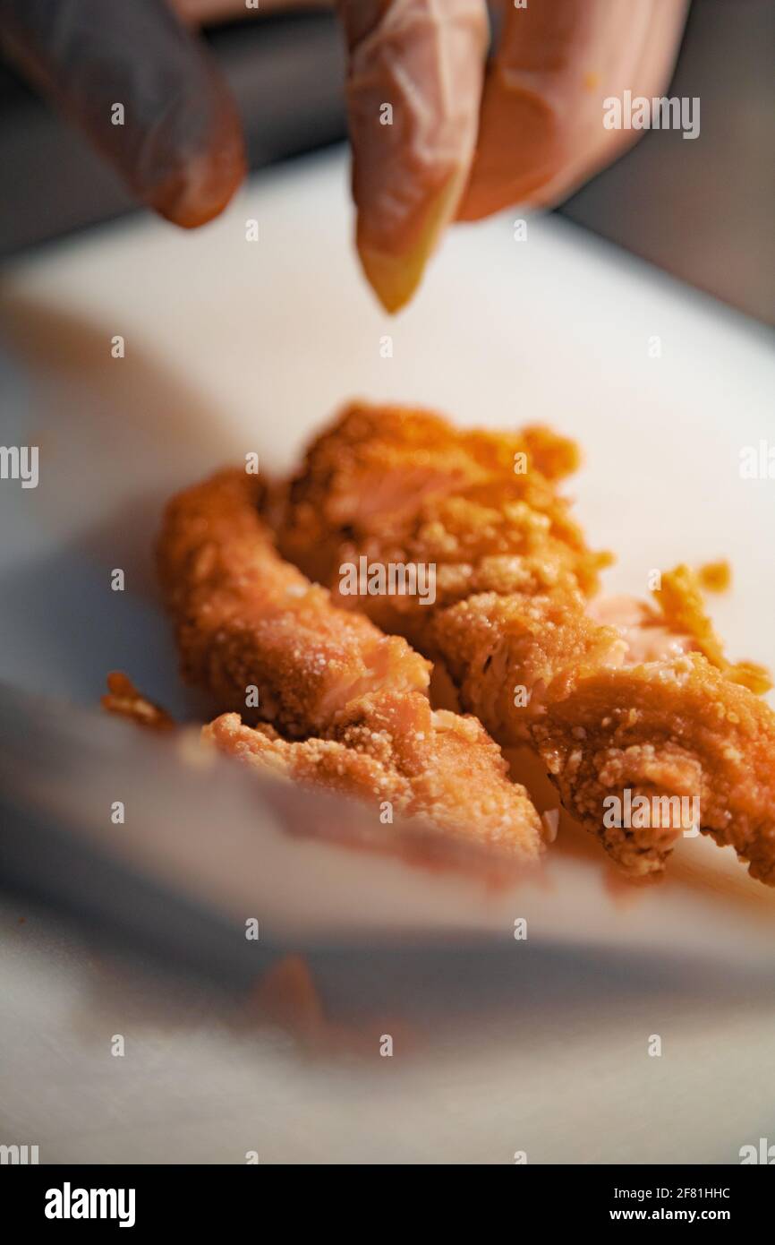 A white gloved chef's hand holding a knife with fried chicken on top of ...