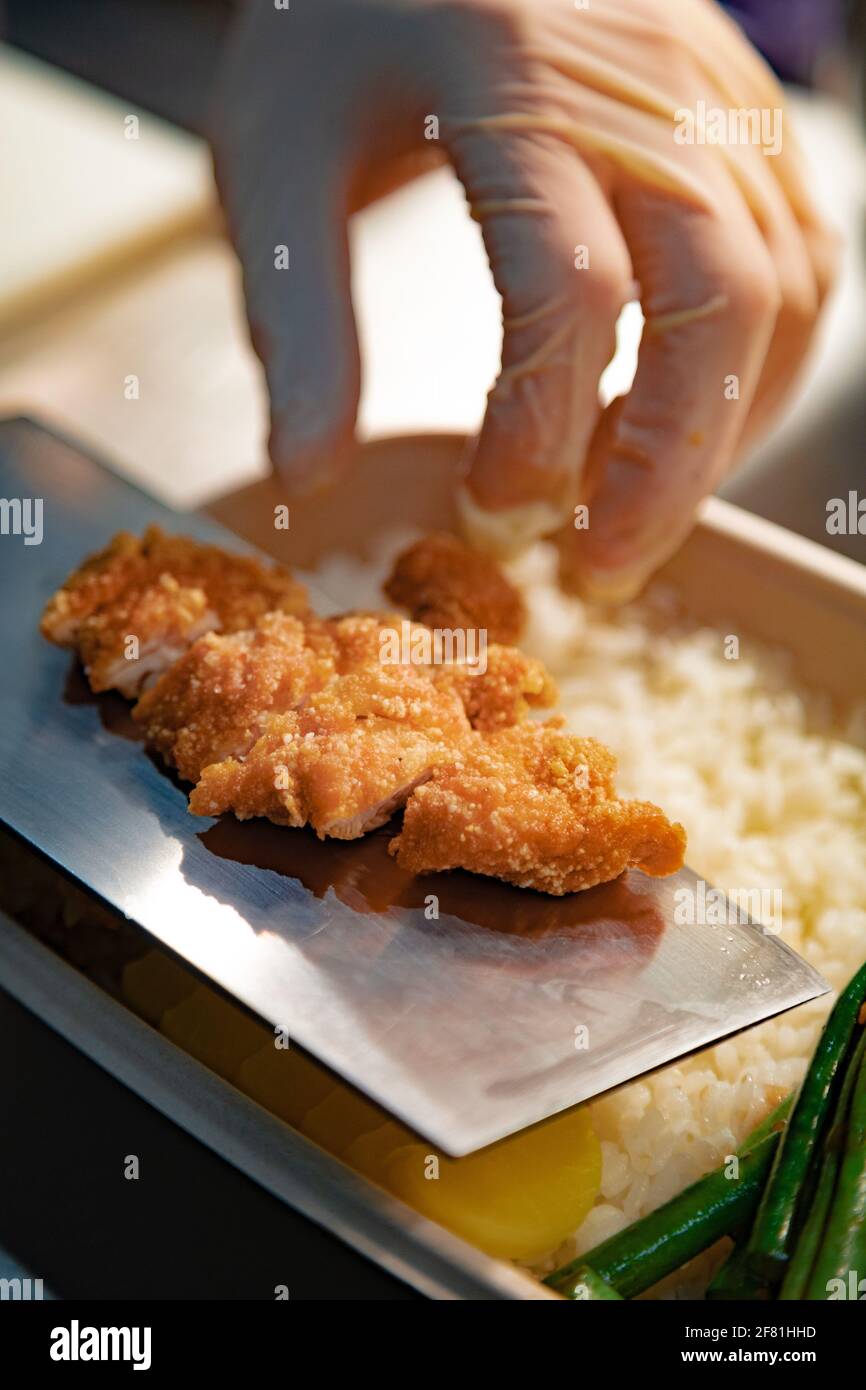 A white gloved chef's hand holding a knife with fried chicken on top of ...