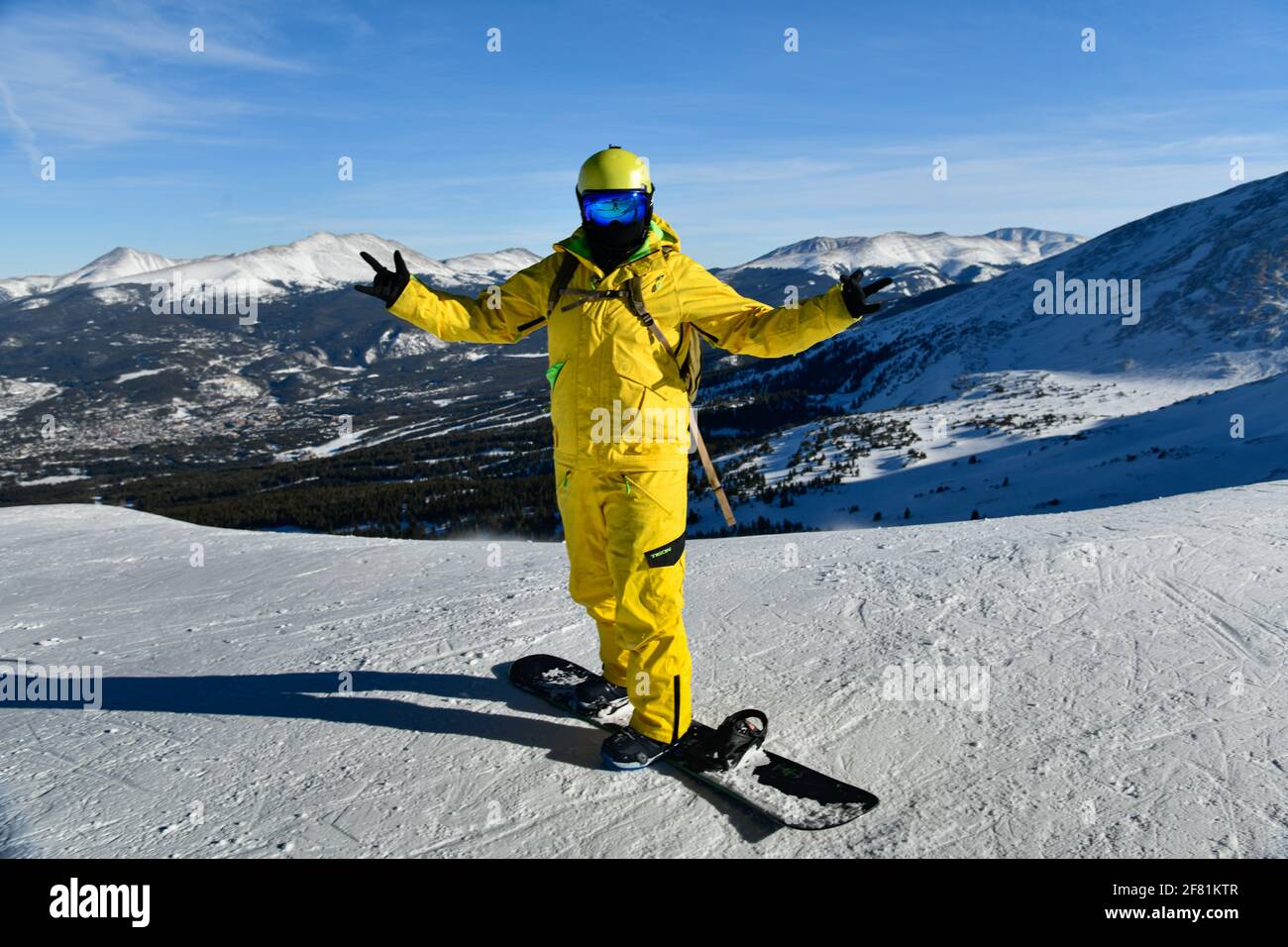 Snowboarder in bright yellow suit posing at the top of the mountain ...