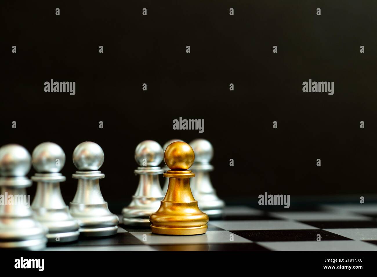Gold pawn piece stand in fron of silver pawn team on black background ...