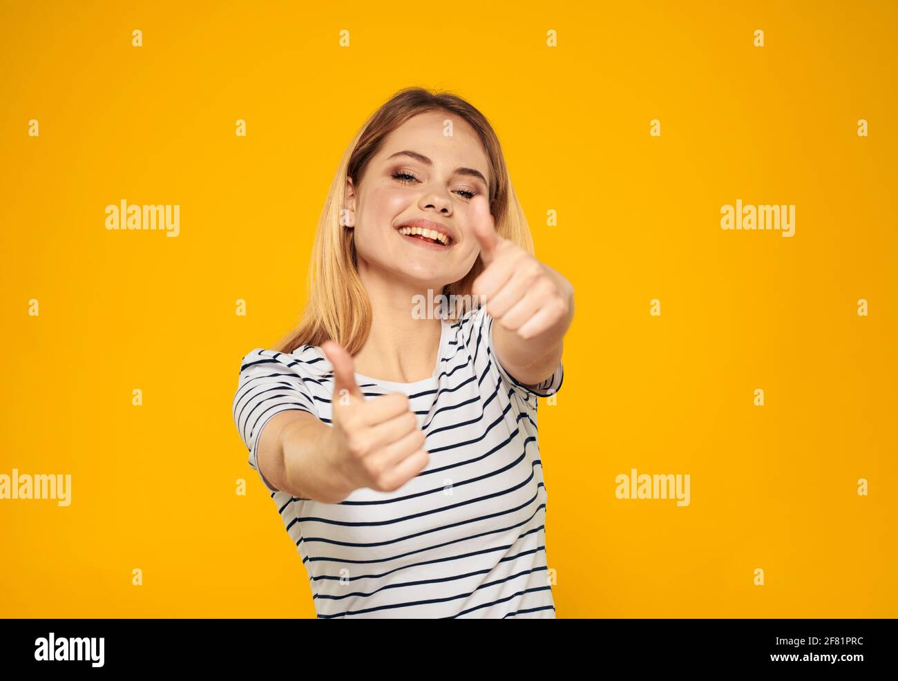 Enthusiastic blonde woman in a striped T-shirt on a yellow background ...
