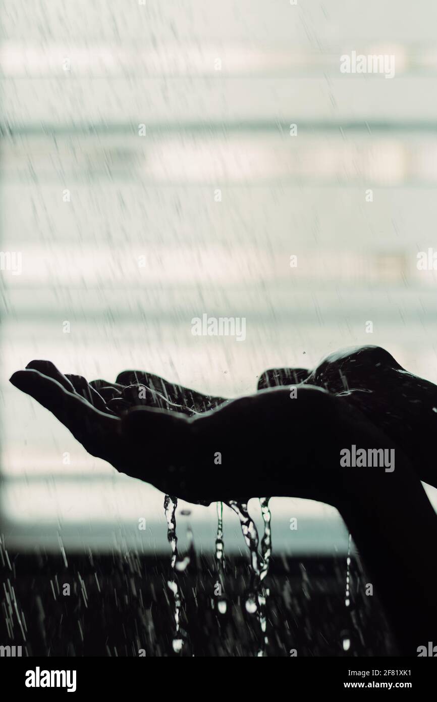 Silhouette of a man's hand under a shower against a backlit window ...