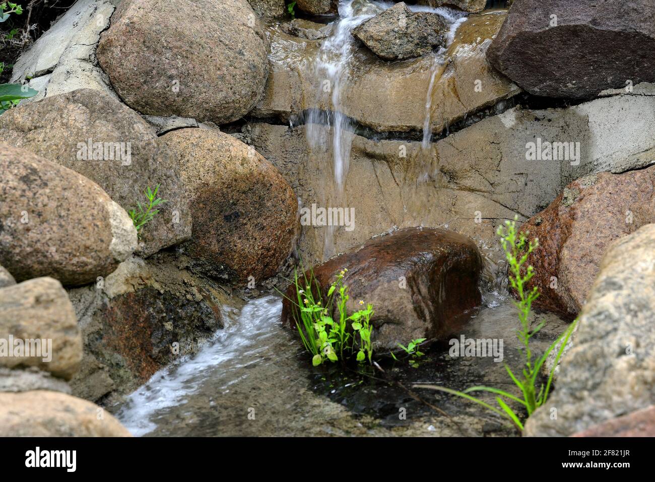 Water cascade built of natural stones and rocks in the backyard garden ...