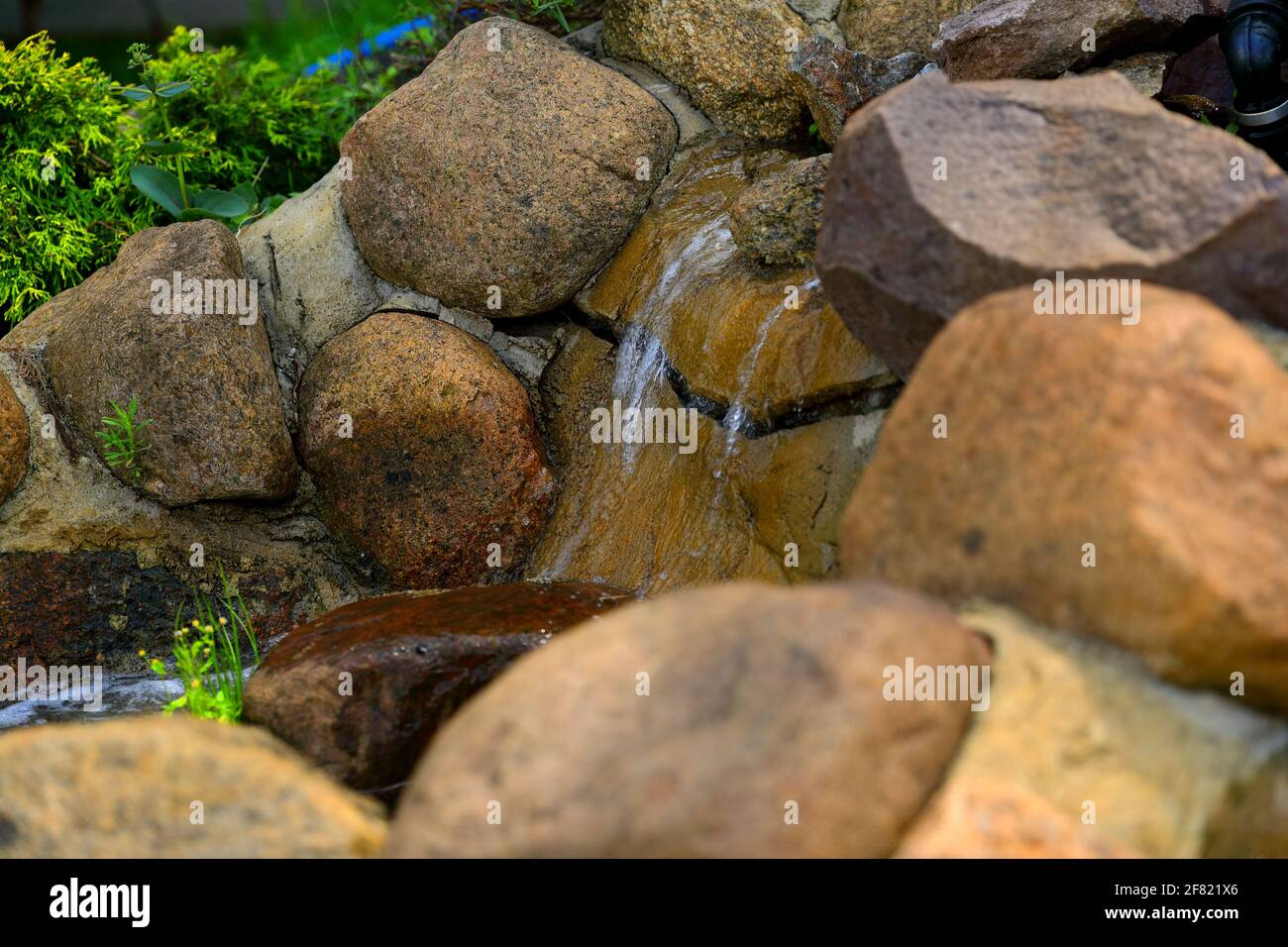Water cascade built of natural stones and rocks in the backyard garden ...
