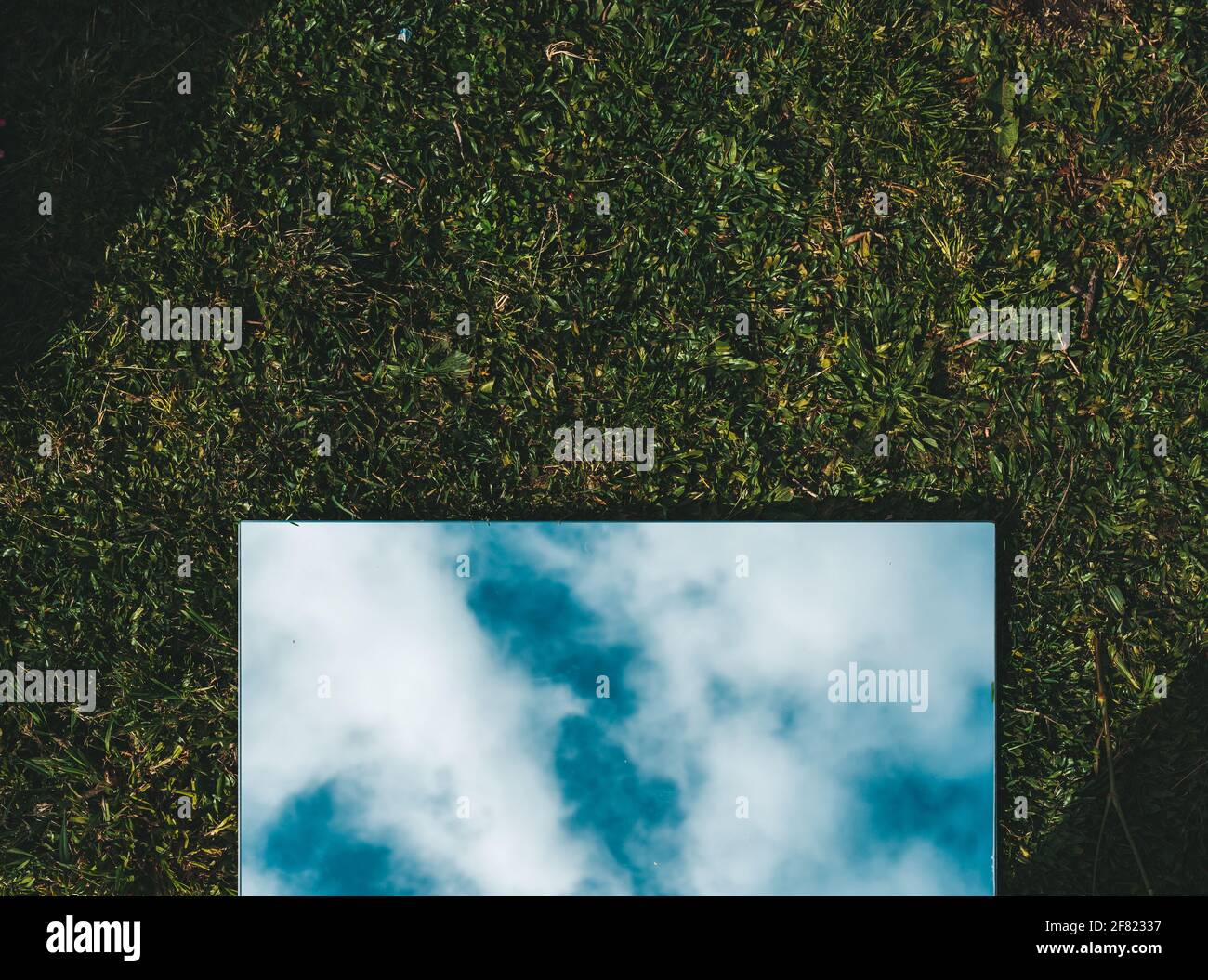 Amazing flat lay of a mirror on the grass, where you can see the clouds ...