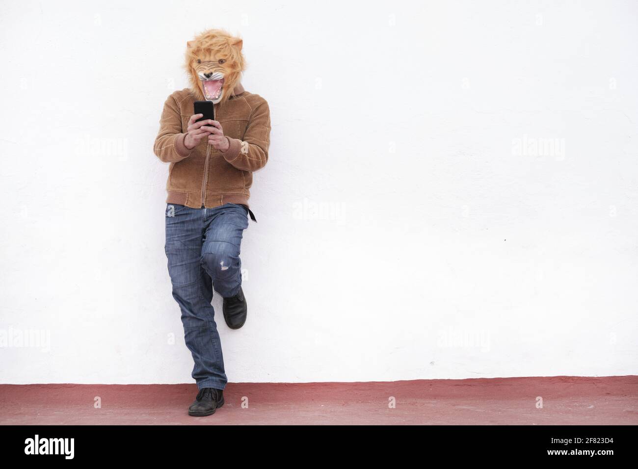 A man with a roaring lion full mask using his phone while leaning ...