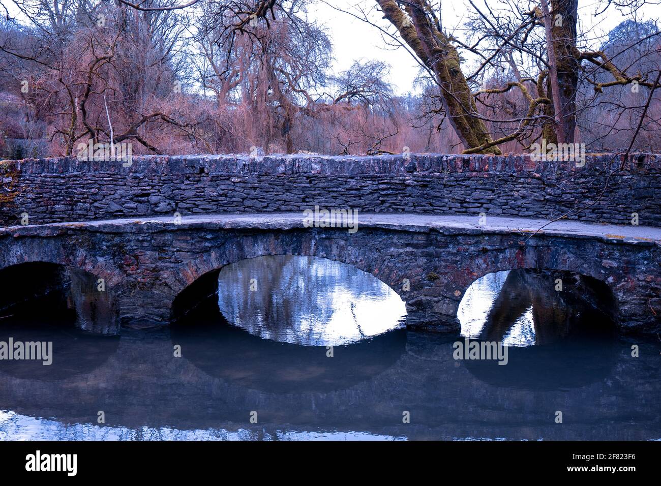 Old stone footbridge over the river Bybrook with reflection of the ...