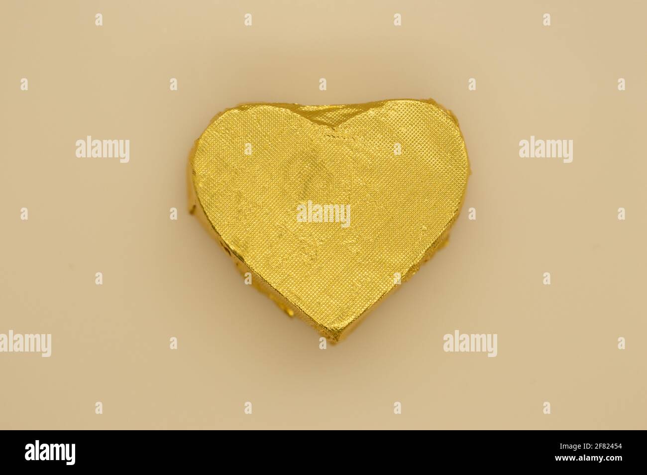 Gold candy wrapper in the shape of a heart on a light beige background ...