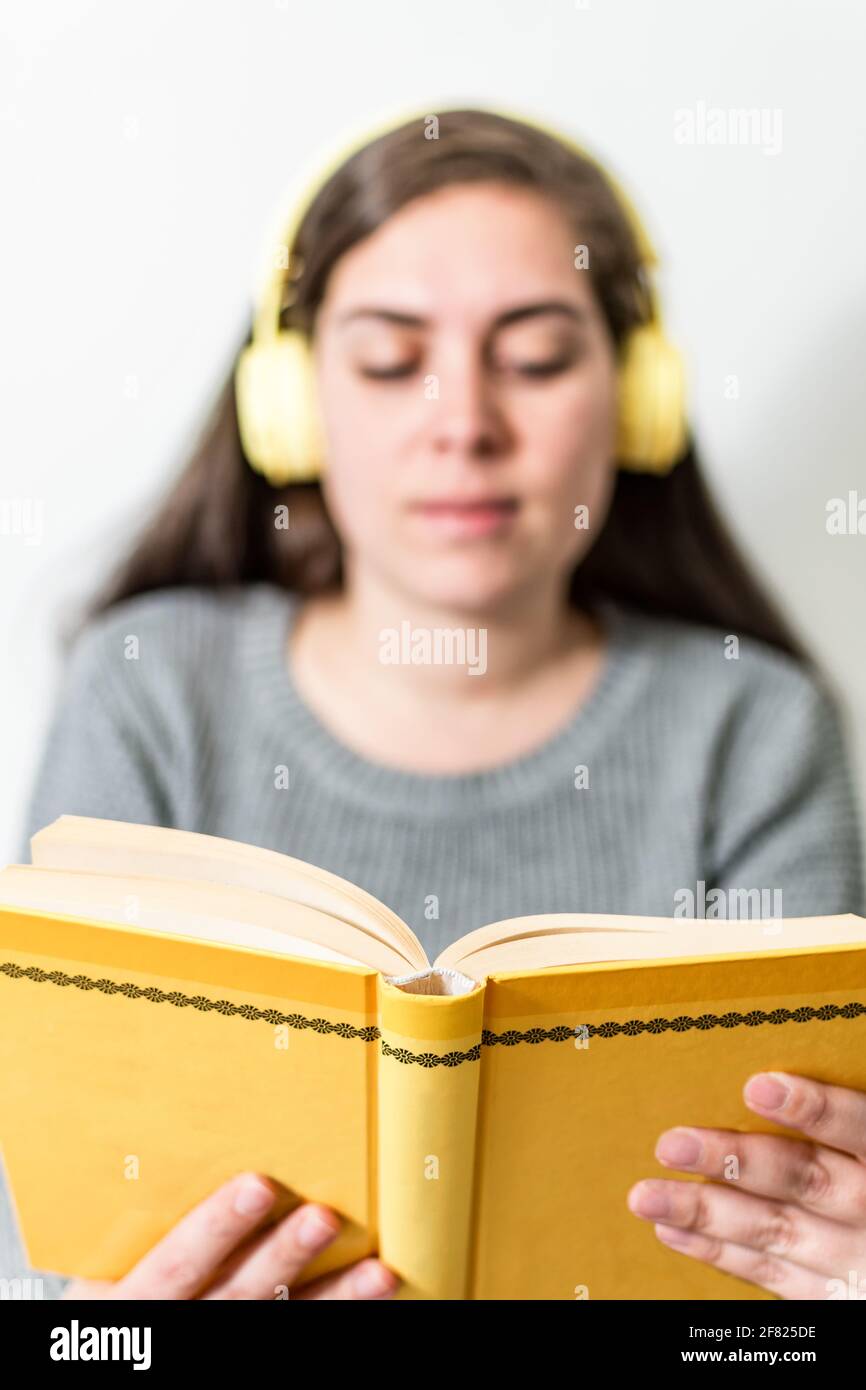 A young Israyeli woman wearing yellow wireless headphones and reading a ...