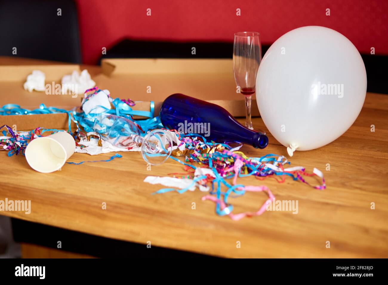 Messy wooden table with pizza box, empty blue bottles, wine glass and ...