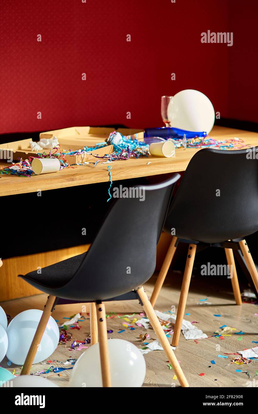Messy wooden table with pizza box, empty blue bottles, wine glass and ...