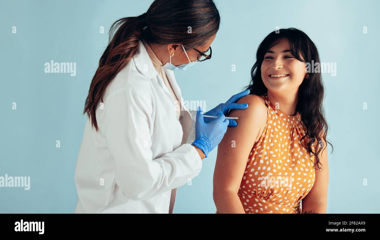 Mature female doctor giving injection to woman on blue background ...