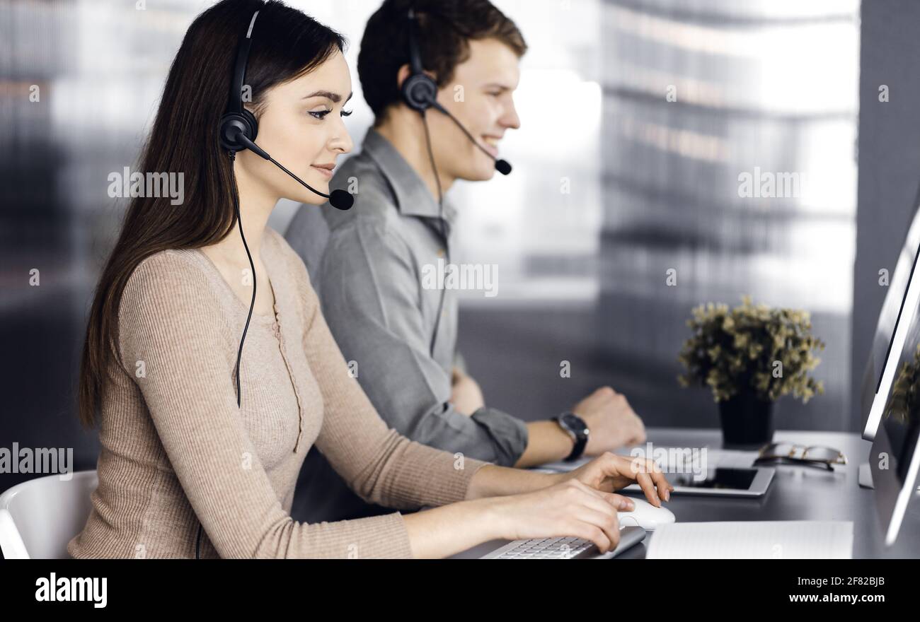 Two young people in headsets are talking to the clients, while sitting ...