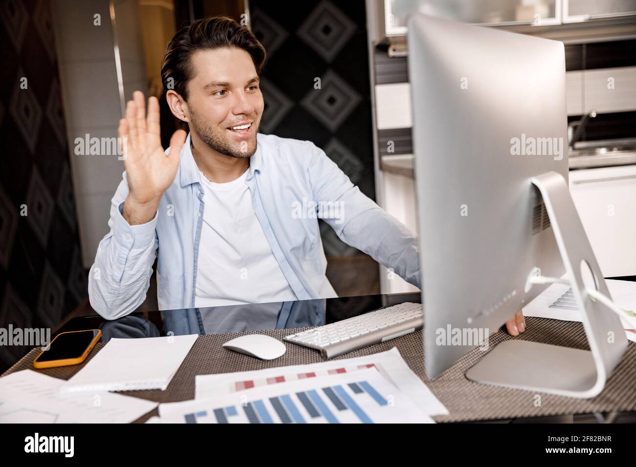 Successful happy businessman is using computer, waving hello to ...