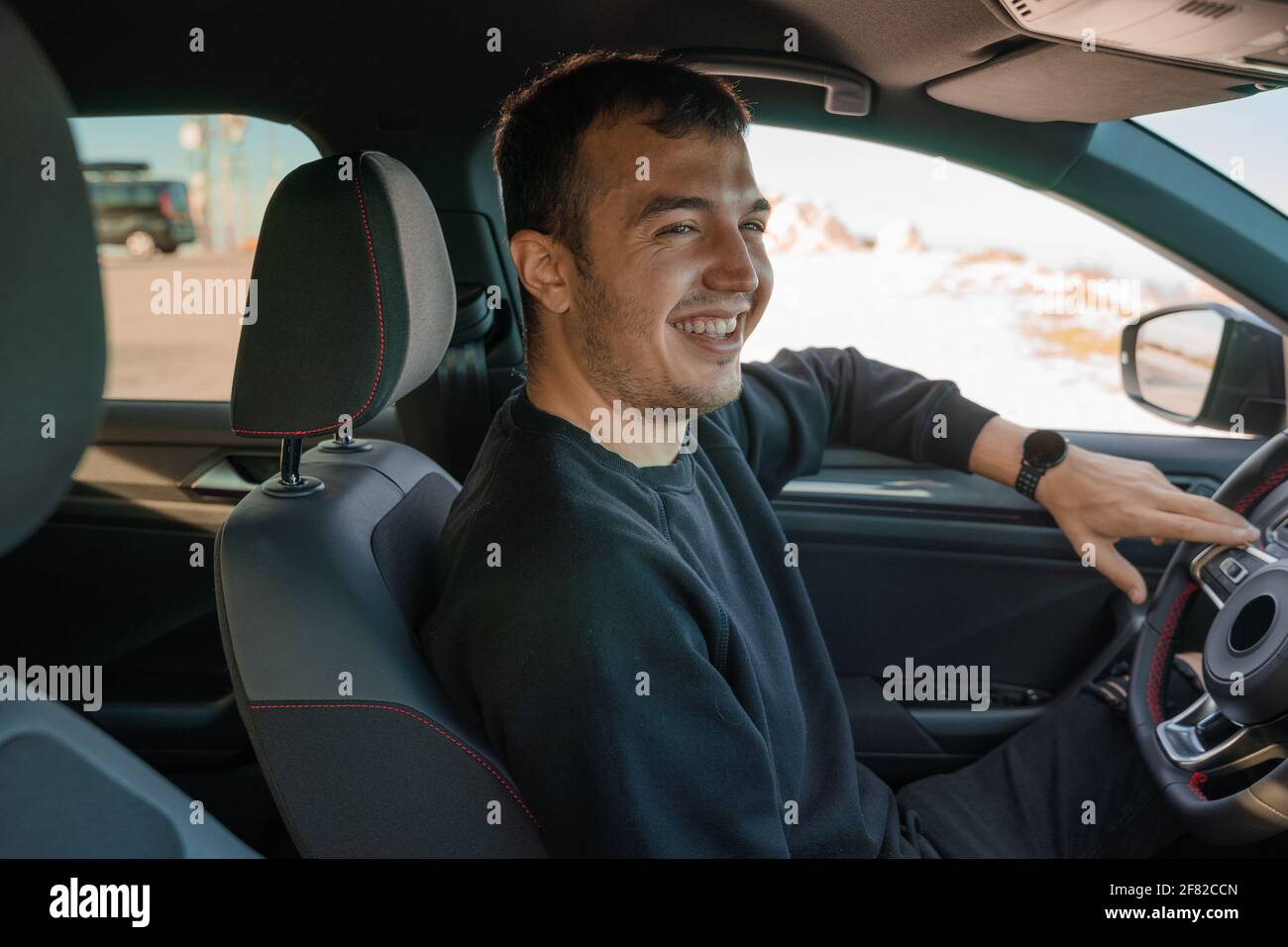 Man inside the car sitting in the driver's seat, smiling with one arm ...
