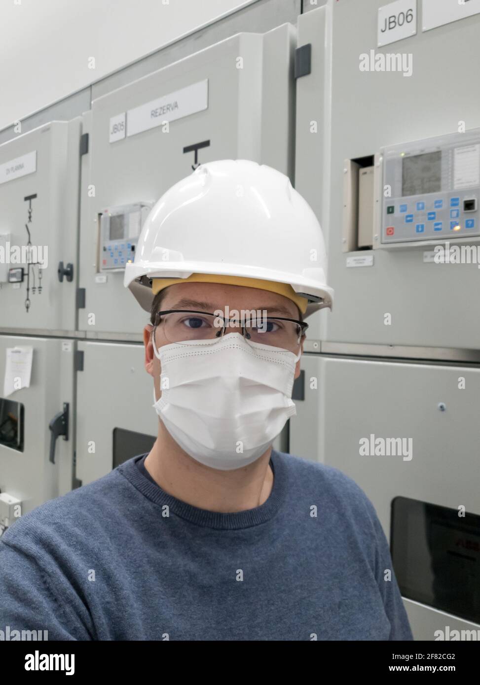 Young engineer working in electrical substation wearing a face mask ...