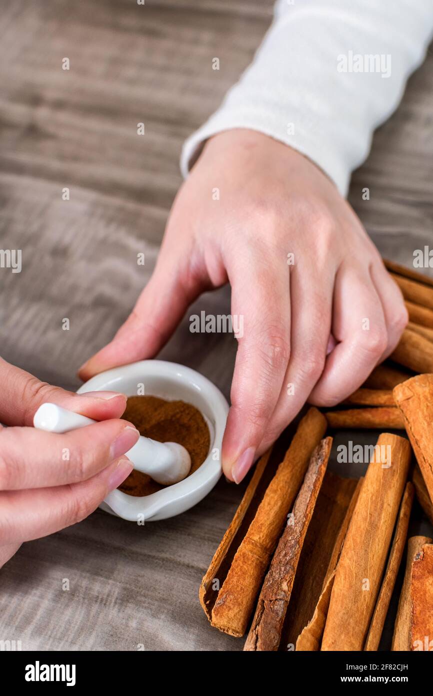A top view of hands grinding cinnamon in a small mortar and pestle ...