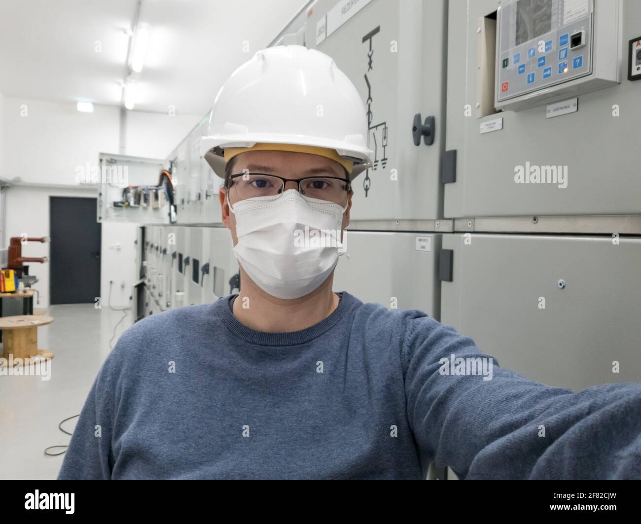Young engineer working in electrical substation wearing a face mask ...