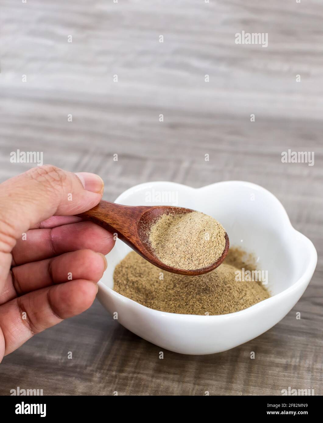 A closeup of a hand holding a wooden spoon with black pepper powder ...